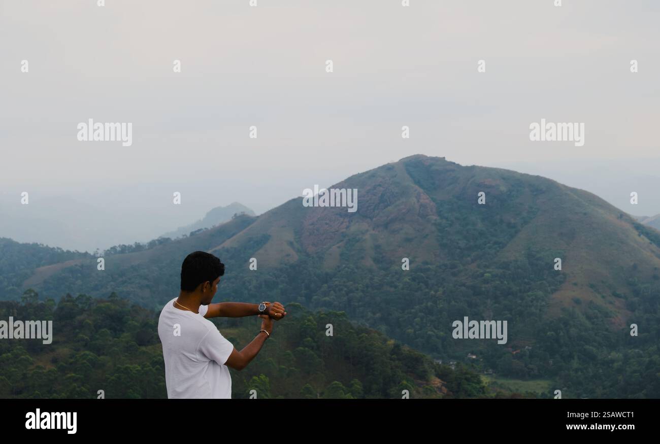 A young man stands triumphantly on a mountain peak, taking in the awe-inspiring landscape Stock ...
