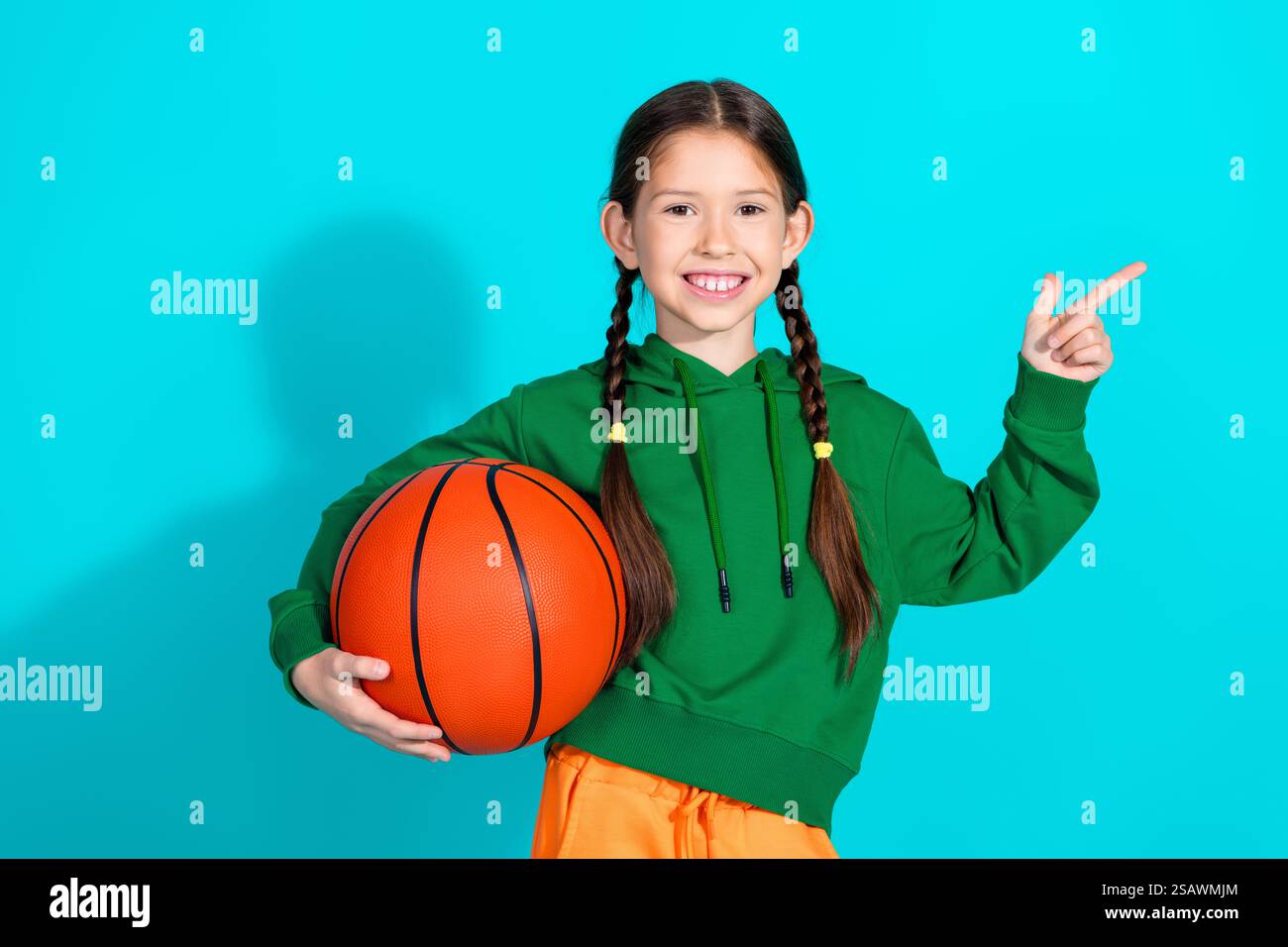 Happy young girl posing with basketball on vibrant turquoise background ...