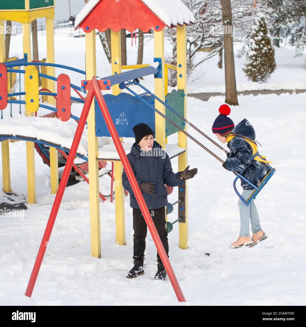 Two children enjoy a snowy winter day at an outdoor playground. One ...