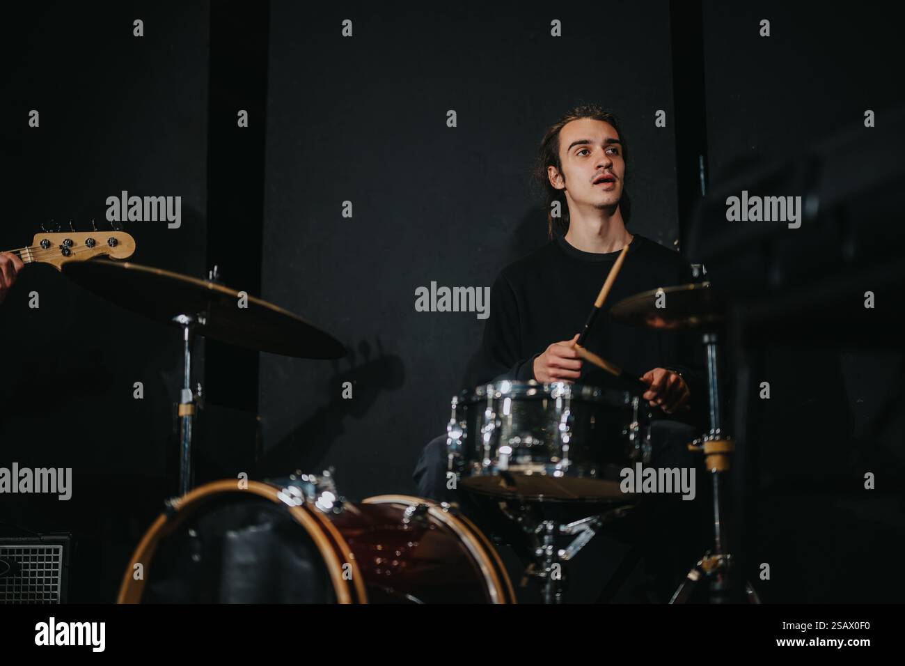 Young drummer practicing in a dimly lit studio setting with instruments ...