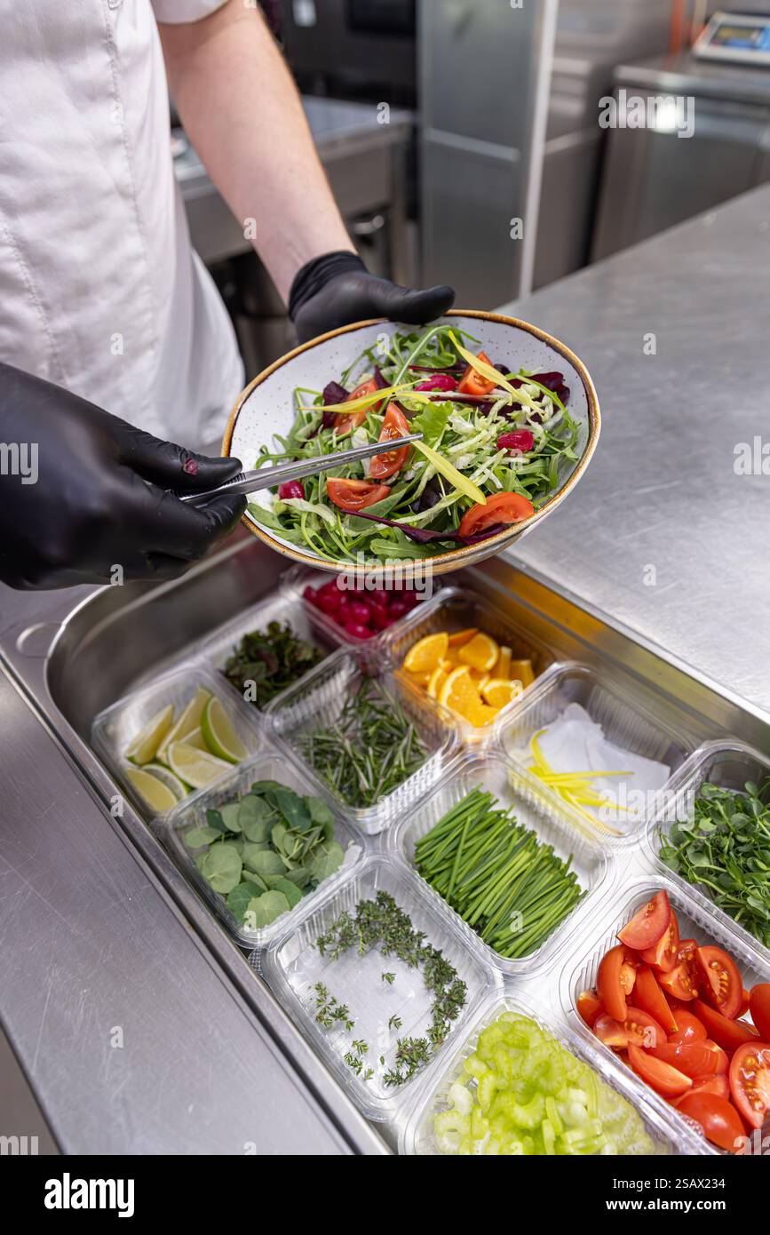 Chef preparing fresh salad in restaurant kitchen using various ...