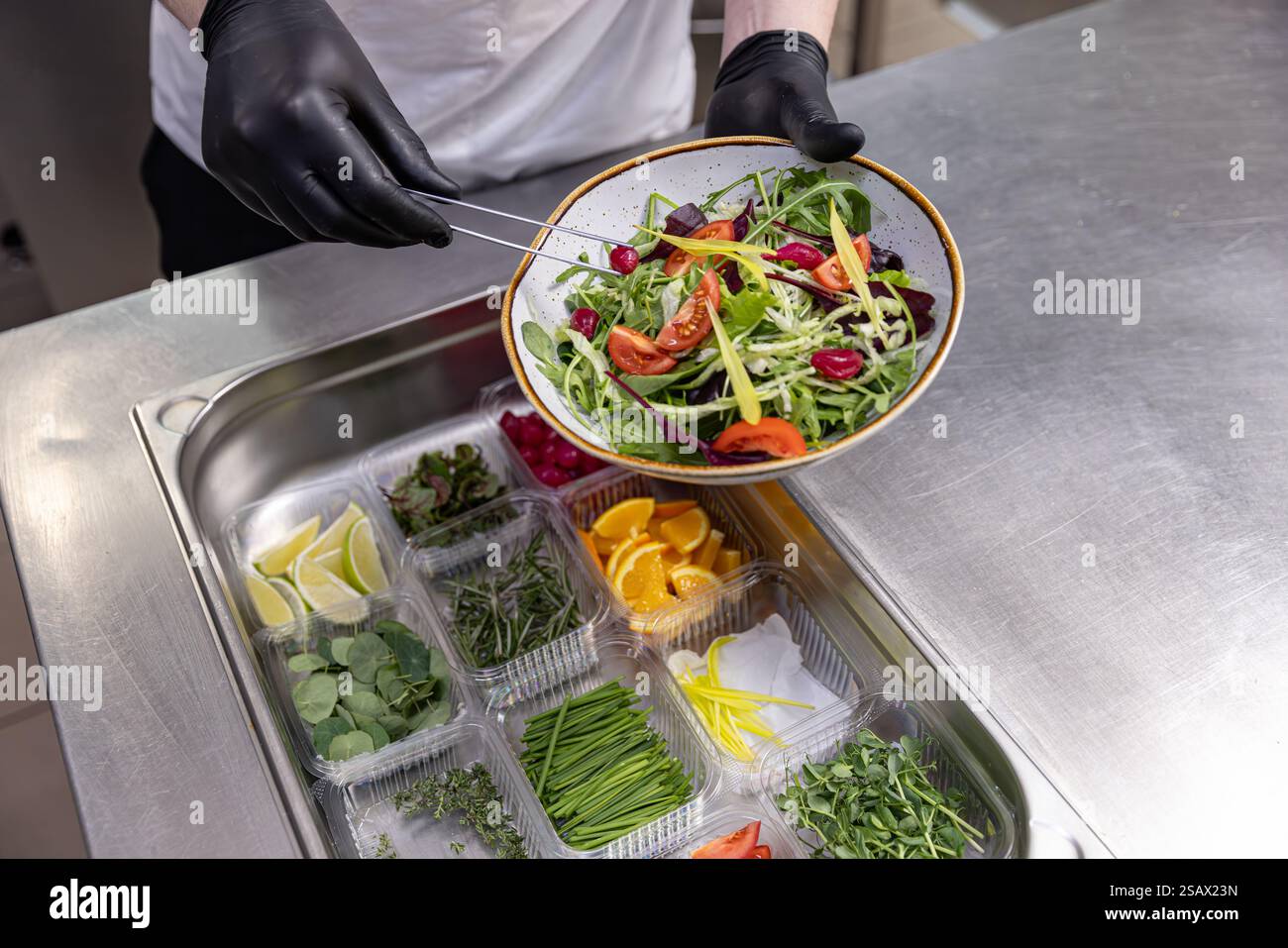 Chef using tongs and holding plate with fresh salad over containers ...