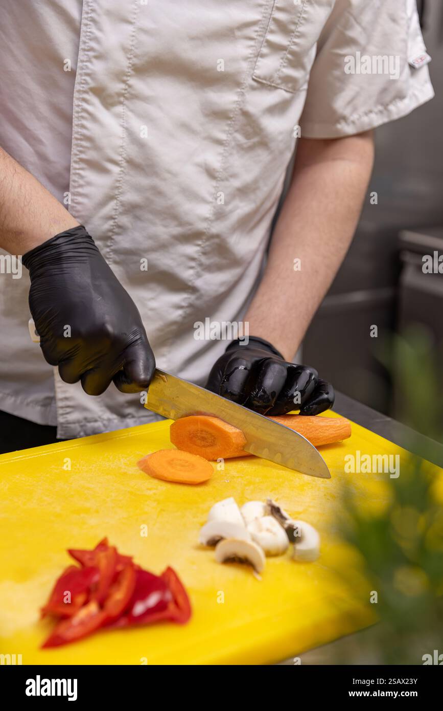 Chef wearing black gloves skillfully slicing fresh carrot, preparing a ...