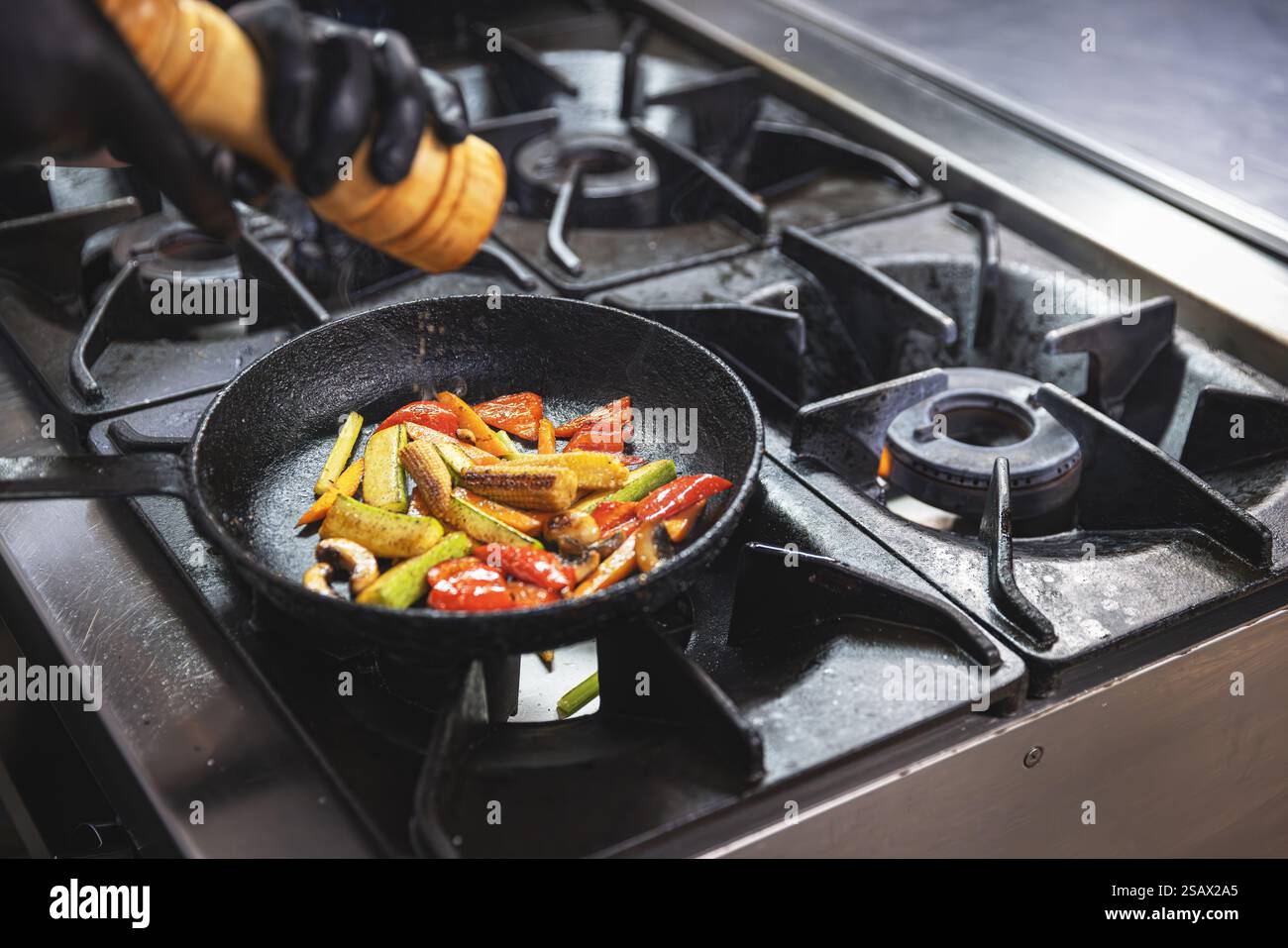Chef adding spices to grilled vegetables in frying pan on gas stove ...