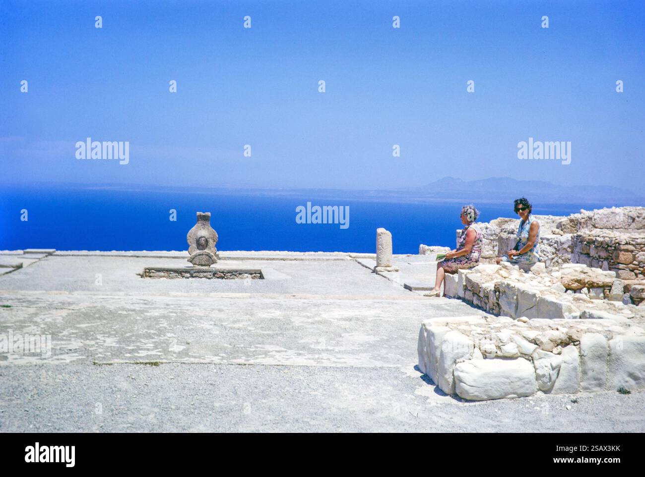 Two women tourists sitting on stone wall at Roman ruins of Vouni Palace ...