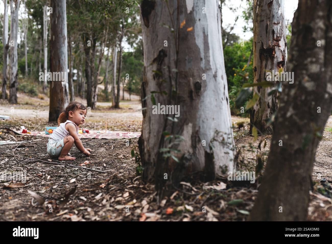 petite baby toddler squats barefoot on earth amongst trees Stock Photo ...