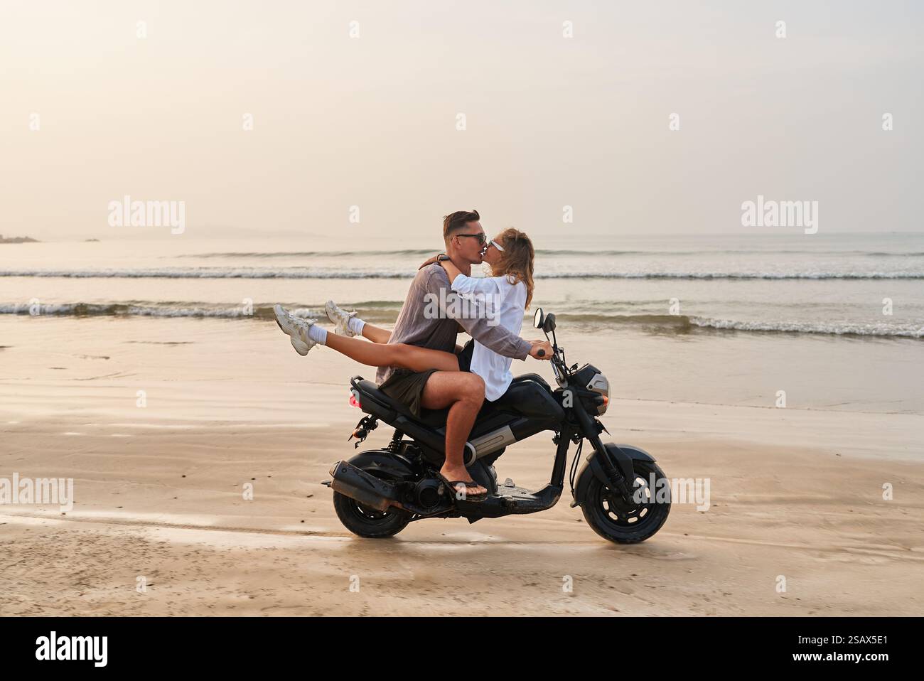 Young couple rides motorbike on beach. Lovers on motorcycle kiss at ...