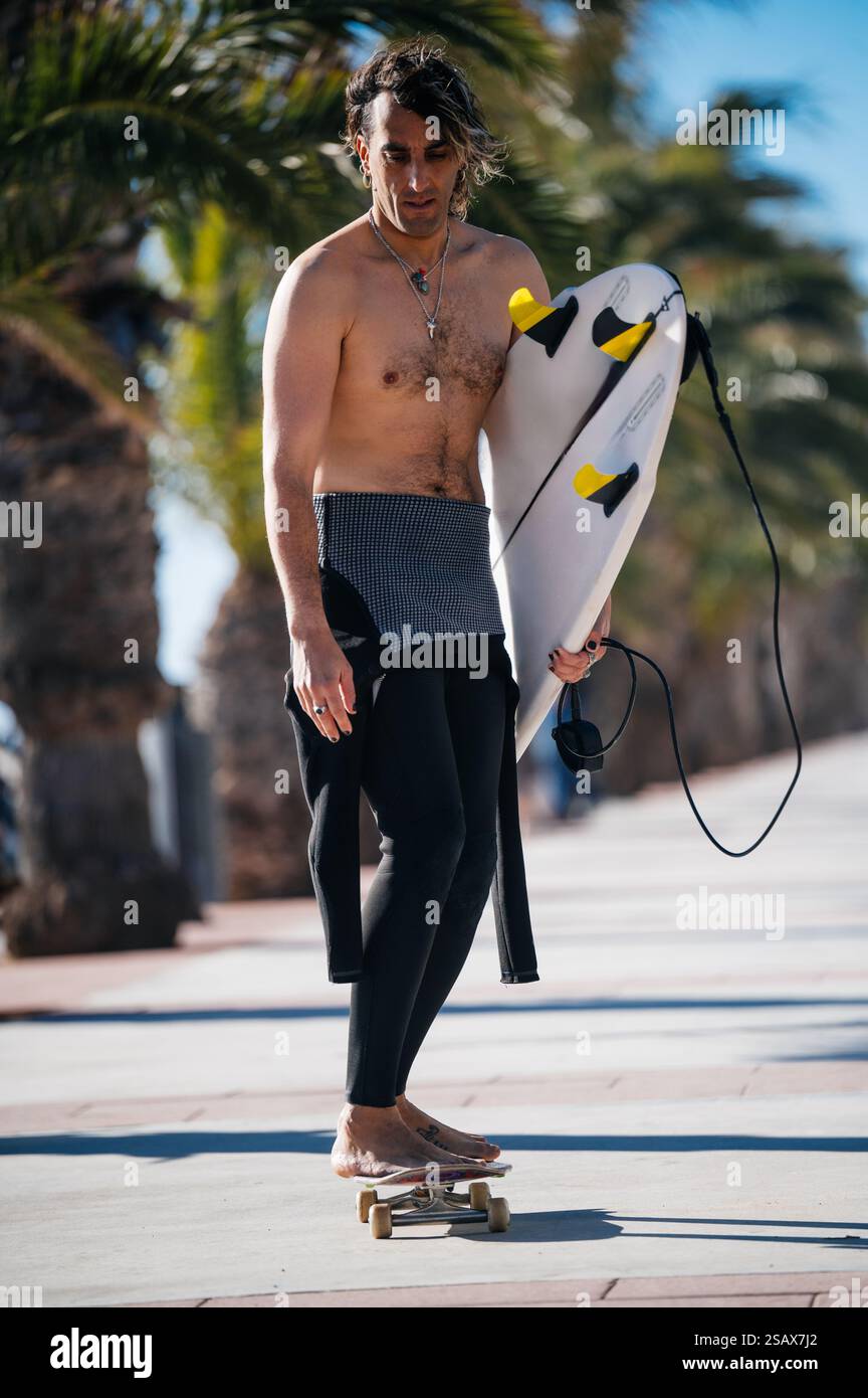Surfer riding skateboard while carrying surfboard on tropical beach ...