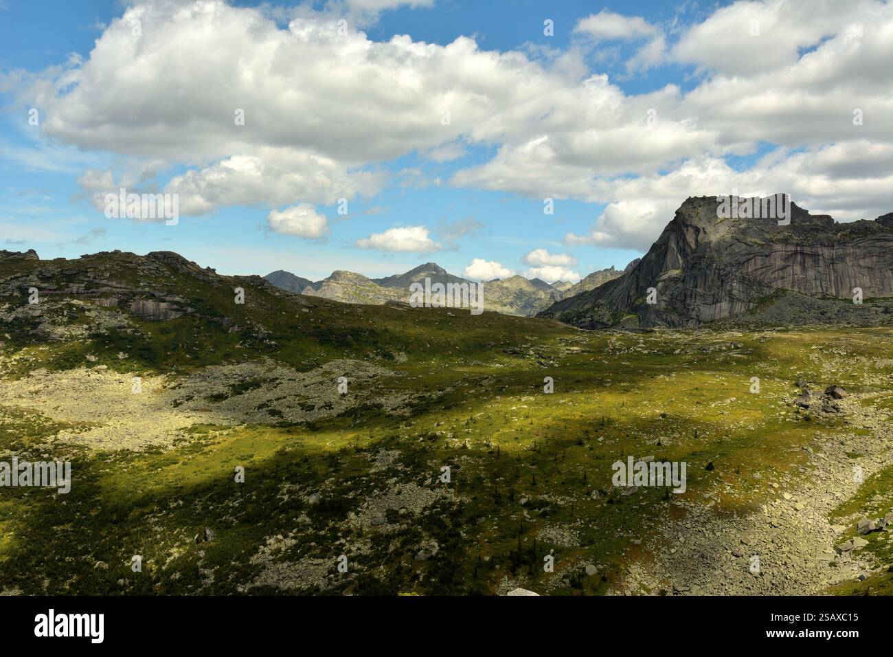 A rocky gentle slope with low grass sandwiched between mountain peaked ...