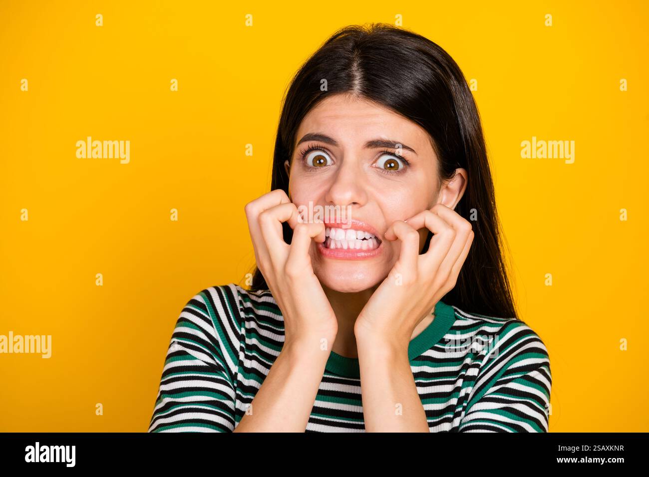 Young woman expressing uncertainty with nervous face, posing against bright yellow background ...