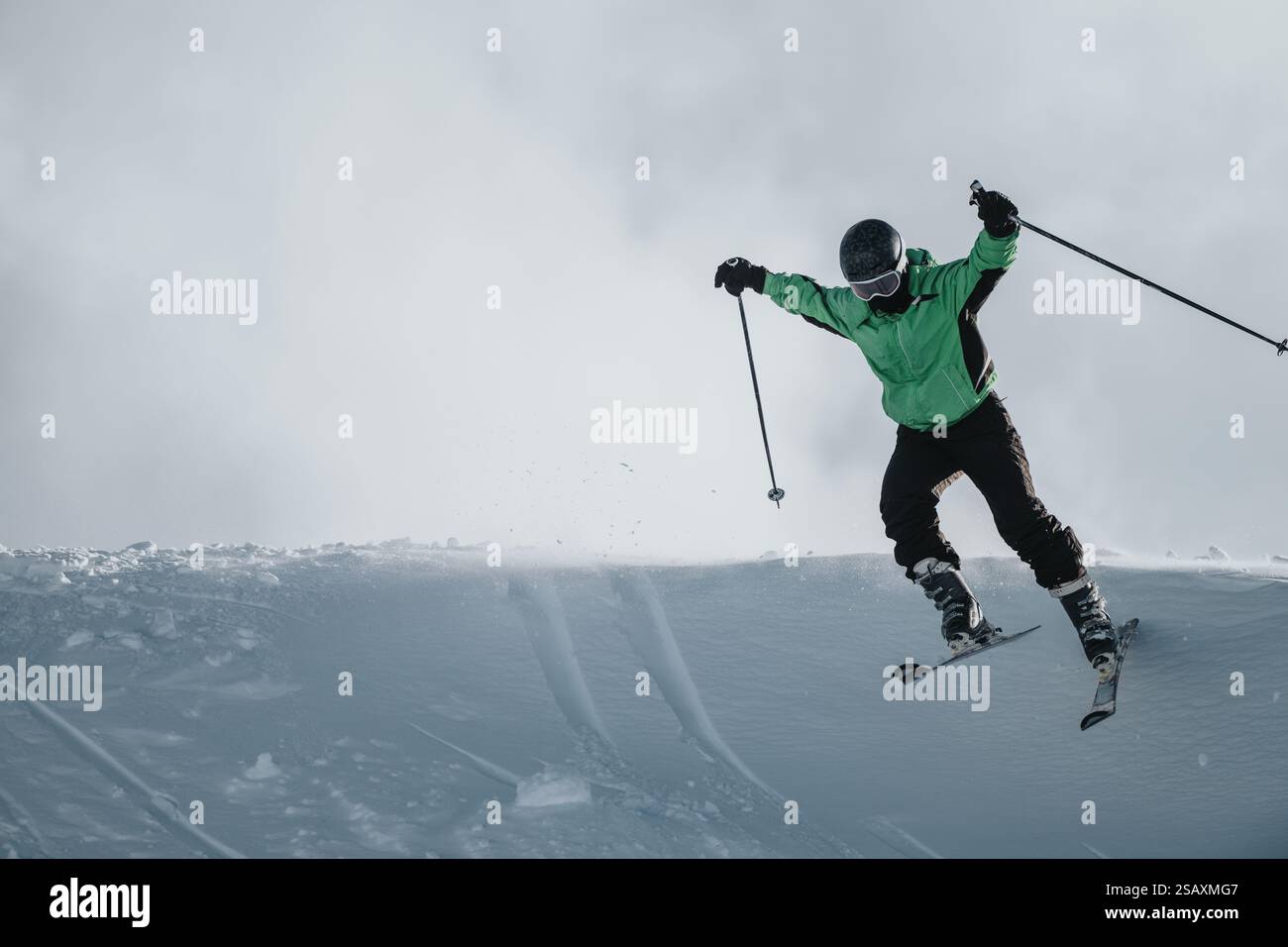 Skier in green jacket performing jump maneuver in snowy mountain ...