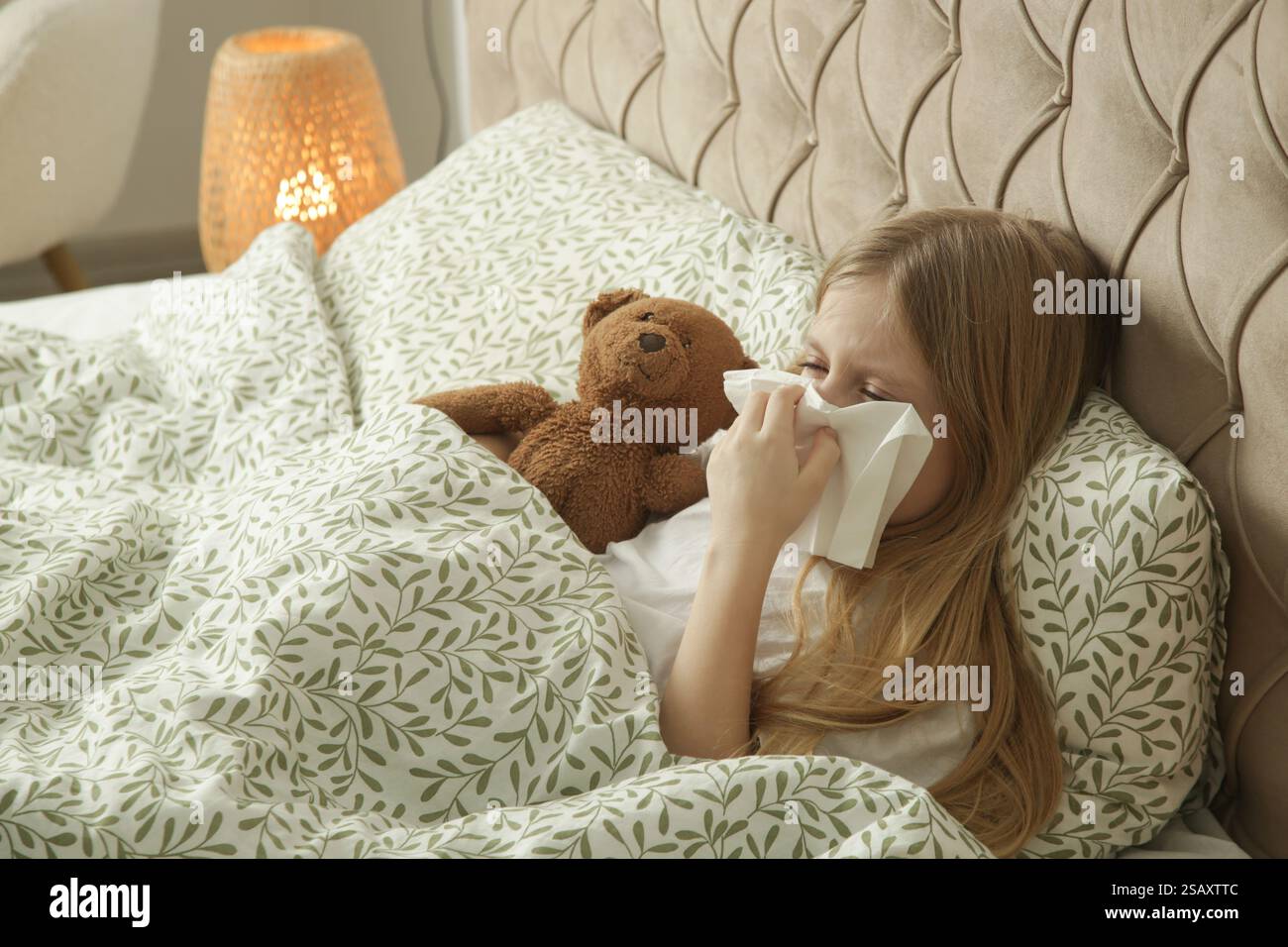 Little 7 year old girl with influenza is sitting in bed and blowing her ...