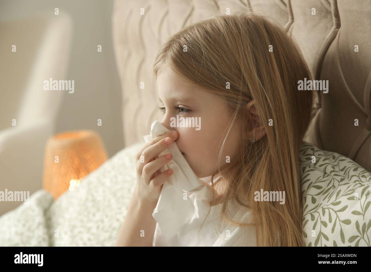 Little 7 year old girl with influenza is sitting in bed and blowing her ...