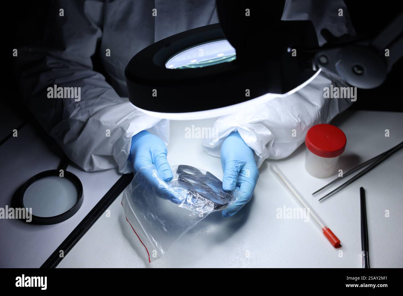 Forensic expert examining evidence in plastic bag at table indoors ...