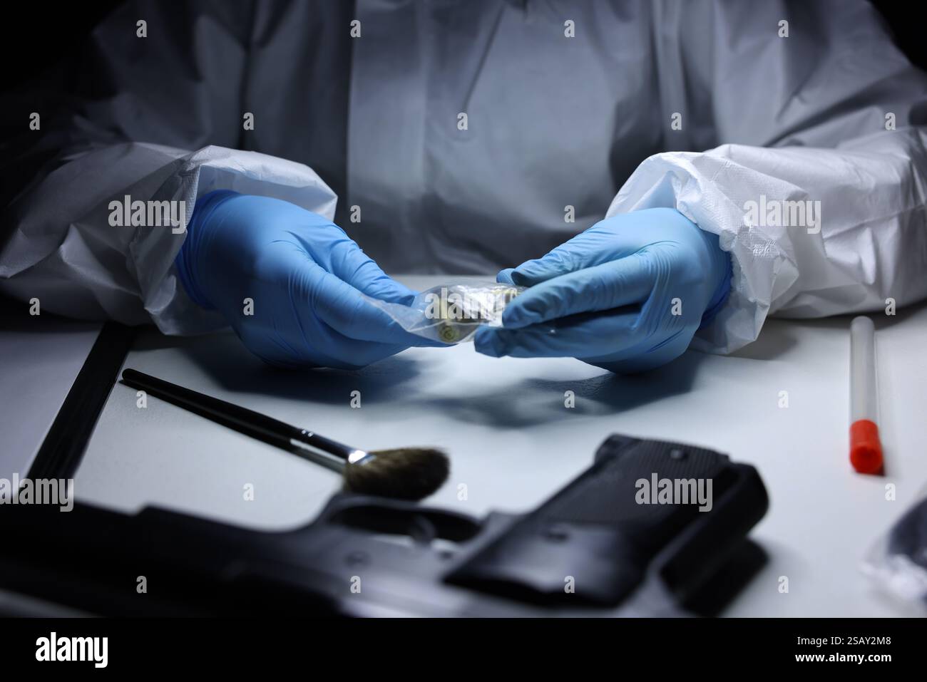 Forensic expert examining shell casings in plastic bag at table indoors ...