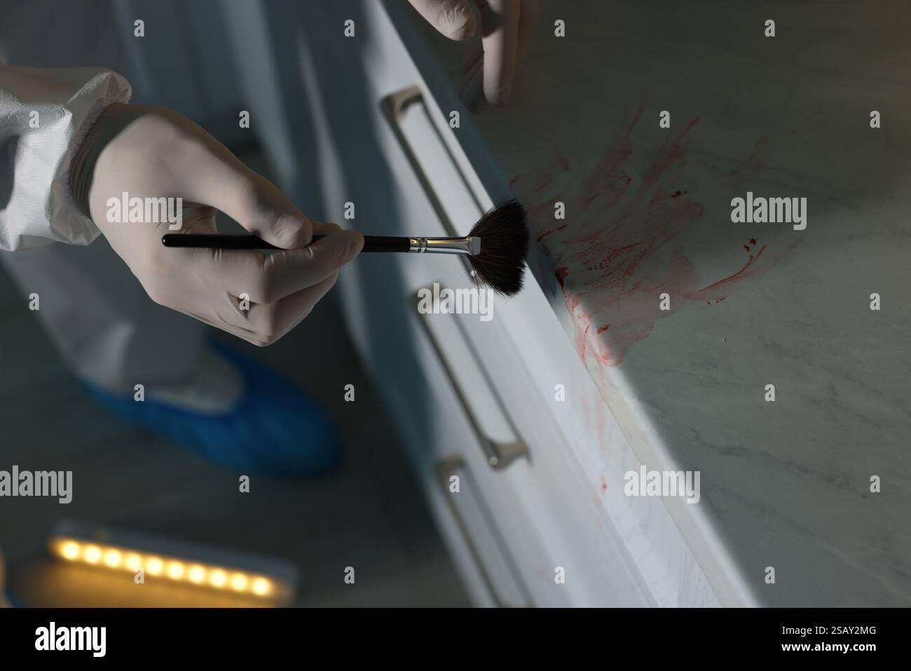 Forensic expert taking fingerprints from countertop with brush at crime scene indoors, closeup ...