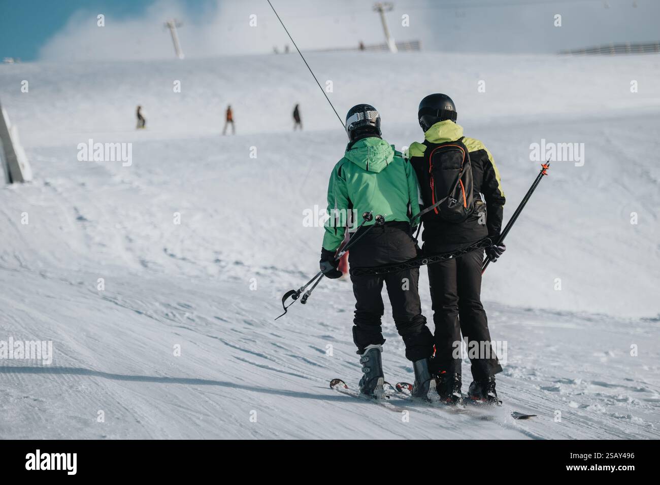 Skiers ascending a snow-covered slope using a ski lift under a clear ...