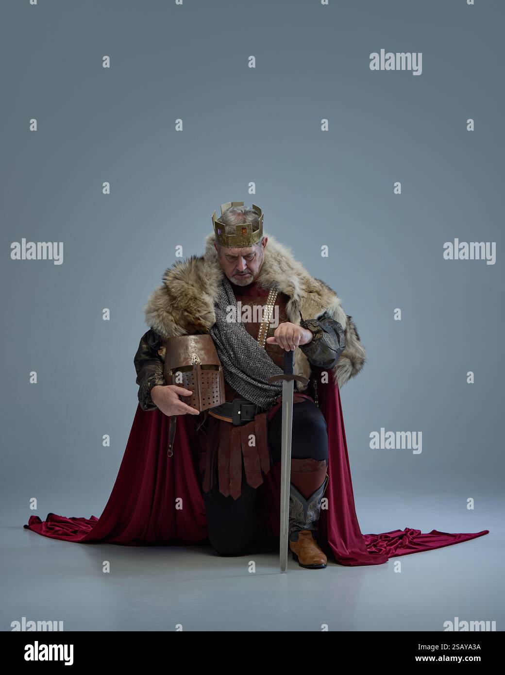 Serious man, medieval king with crown and fur cloak holding metal ...