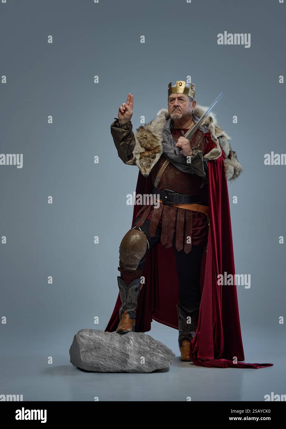Senior serious man as medieval king standing on stone with sword and ...