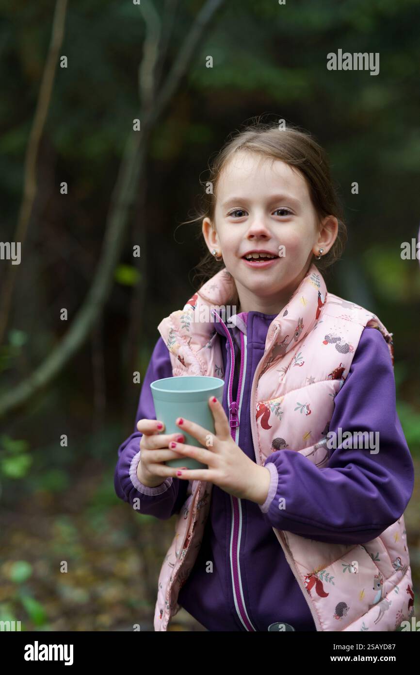Cute beautiful girl in a vest smiling drinking from a plastic cup ...