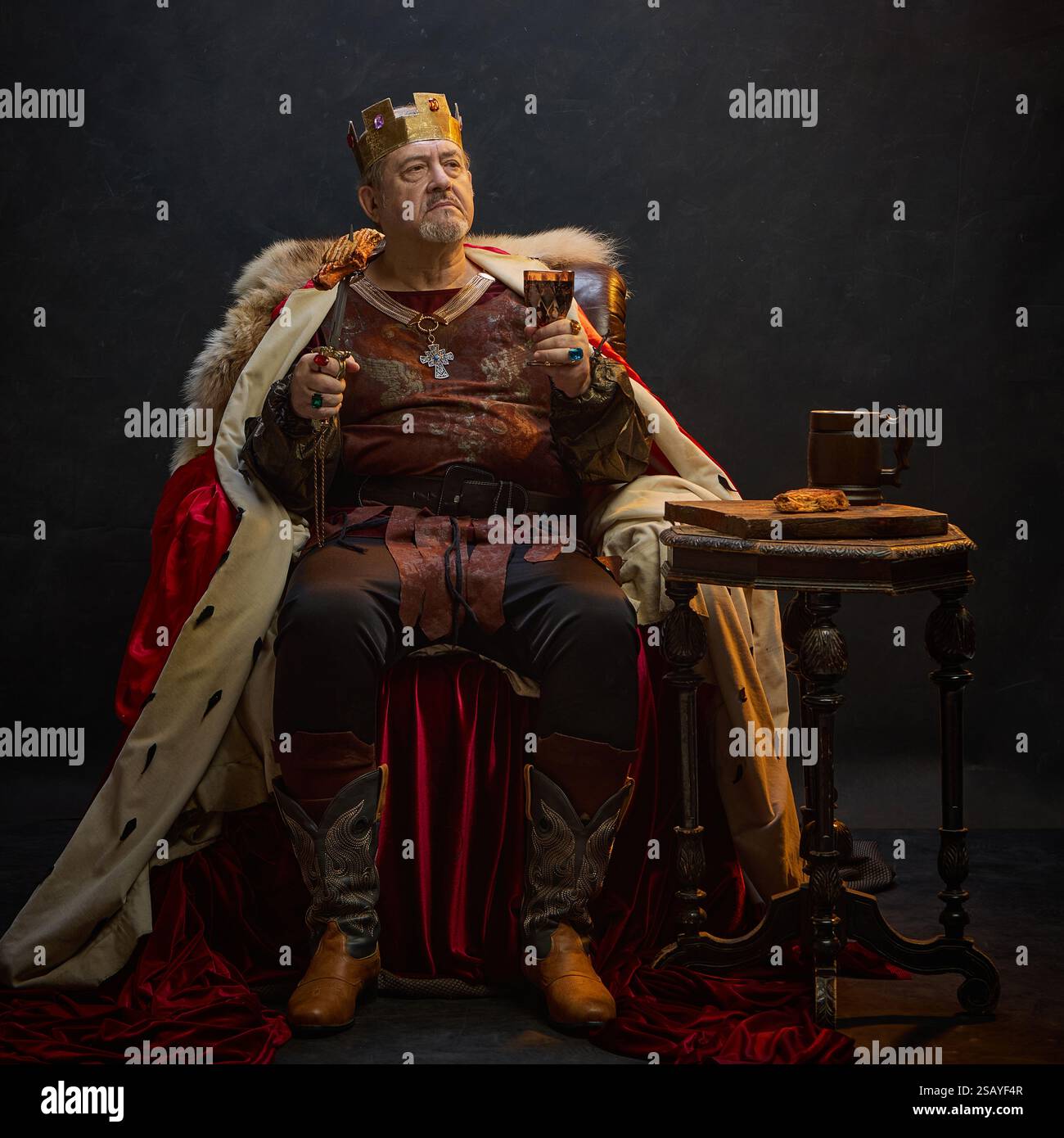 Senior man, medieval king in period attire sitting on throne with meat ...