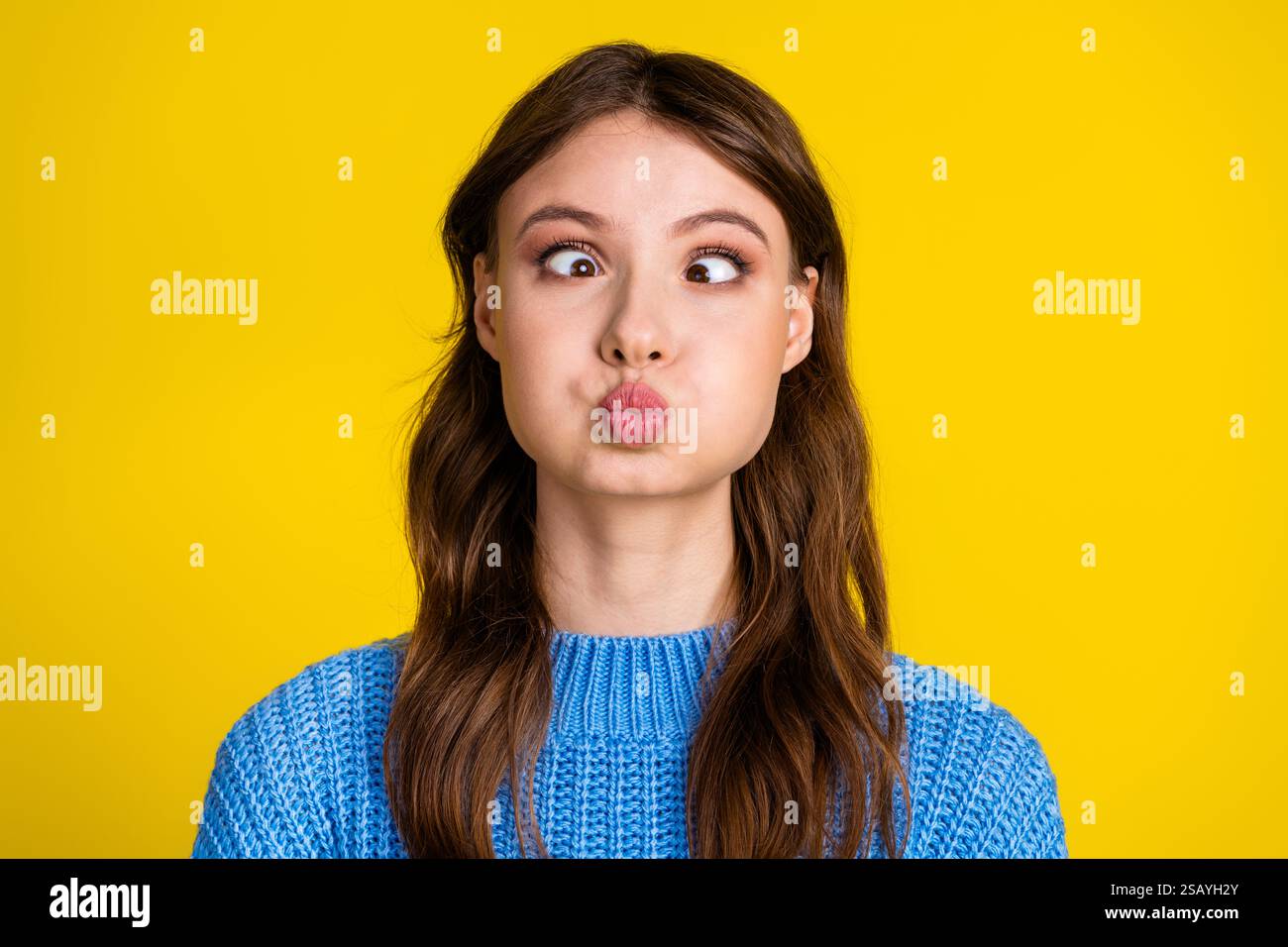 Funny young woman puffing cheeks in a blue sweater against a vibrant ...