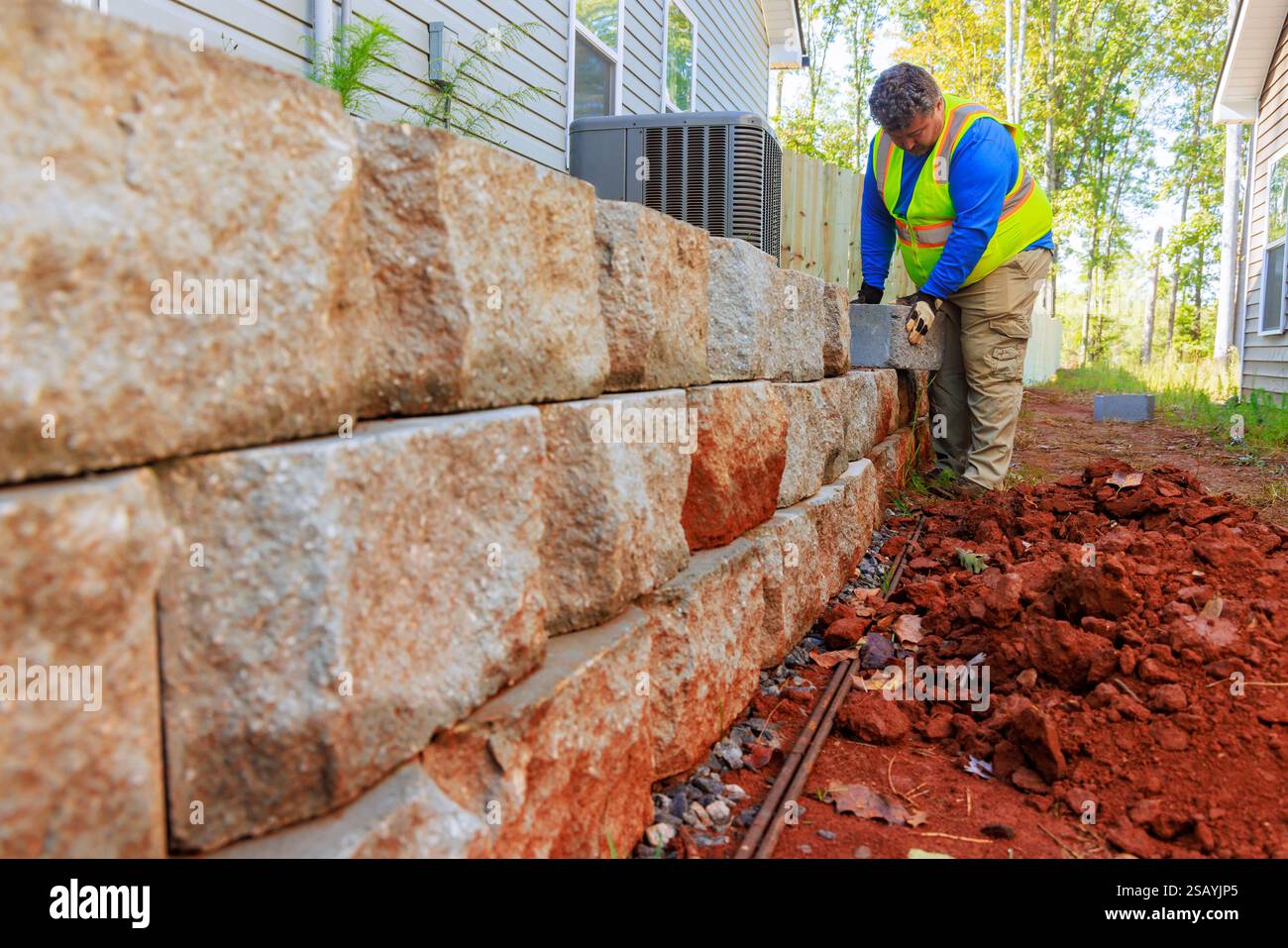 Construction worker carefully places wall stones to form retaining wall ...