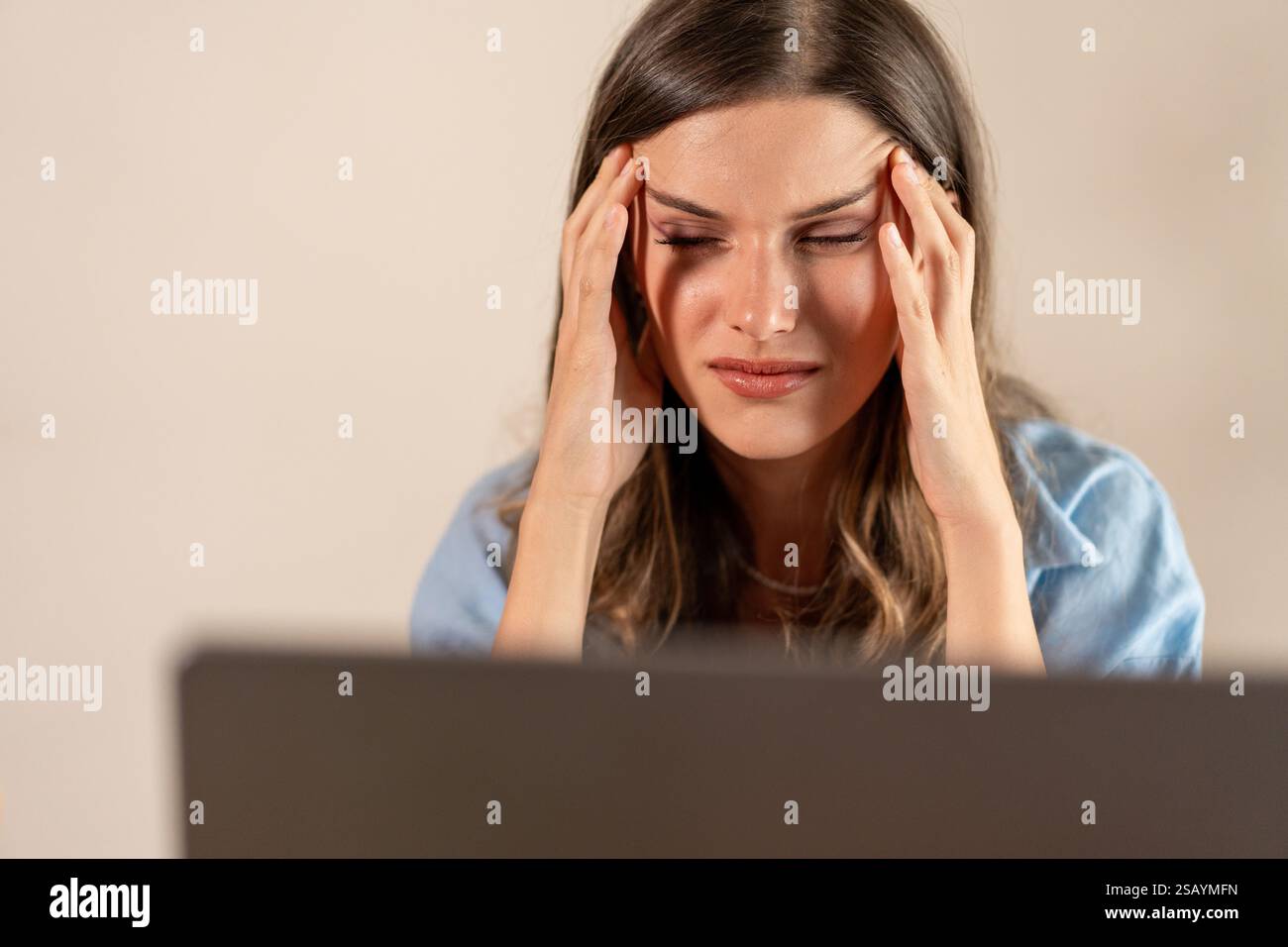 A frustrated woman holding her head while working on a laptop ...