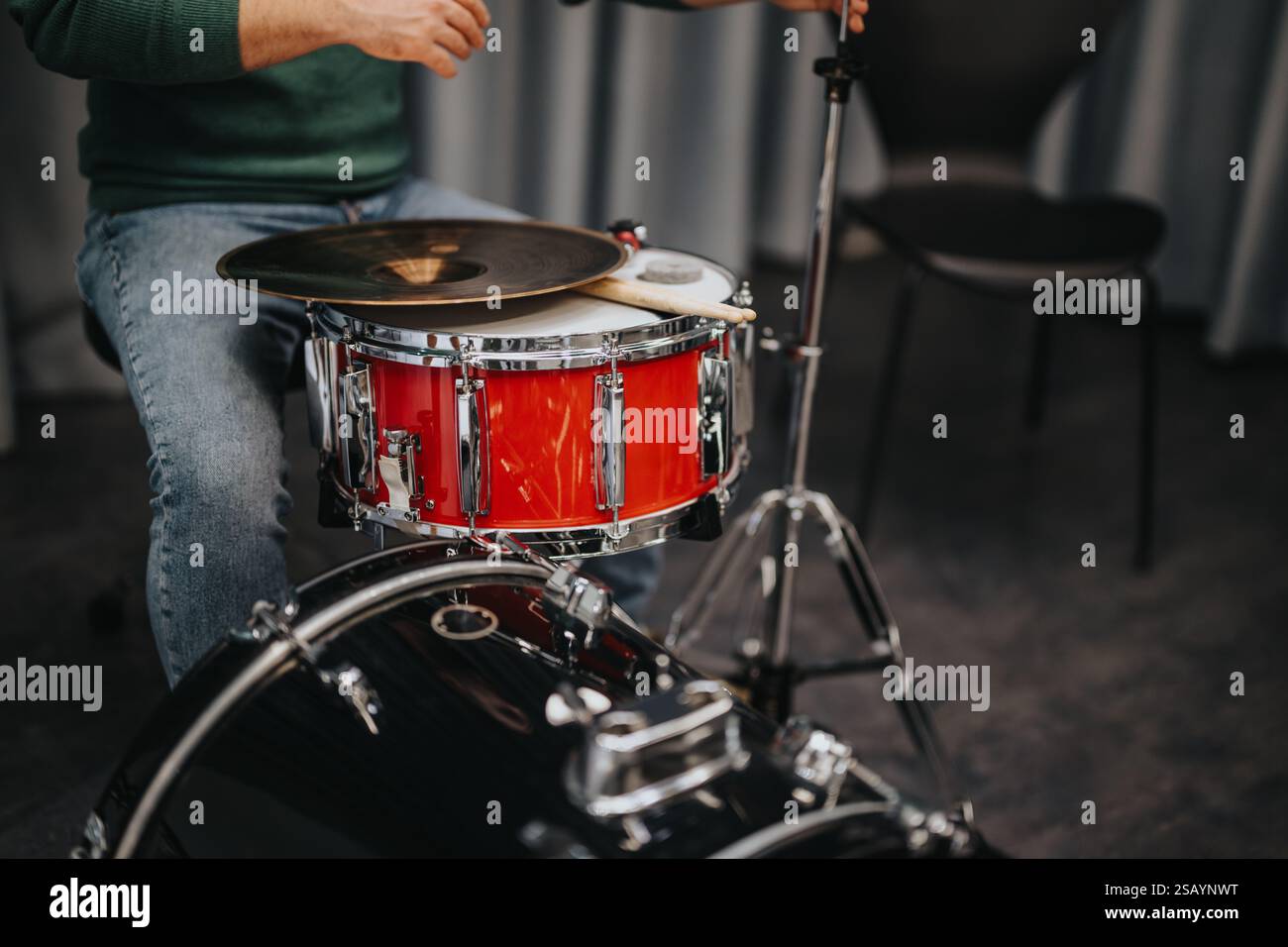 Man playing on a red snare drum with cymbals in a music practice space ...