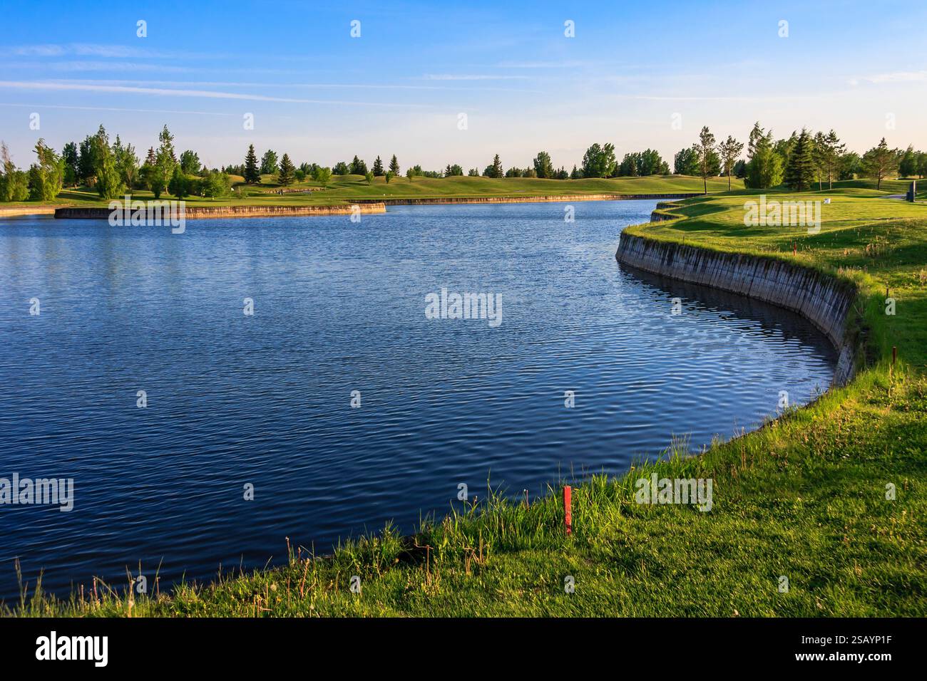 A calm lake with a green grassy shoreline. The water is clear and the ...