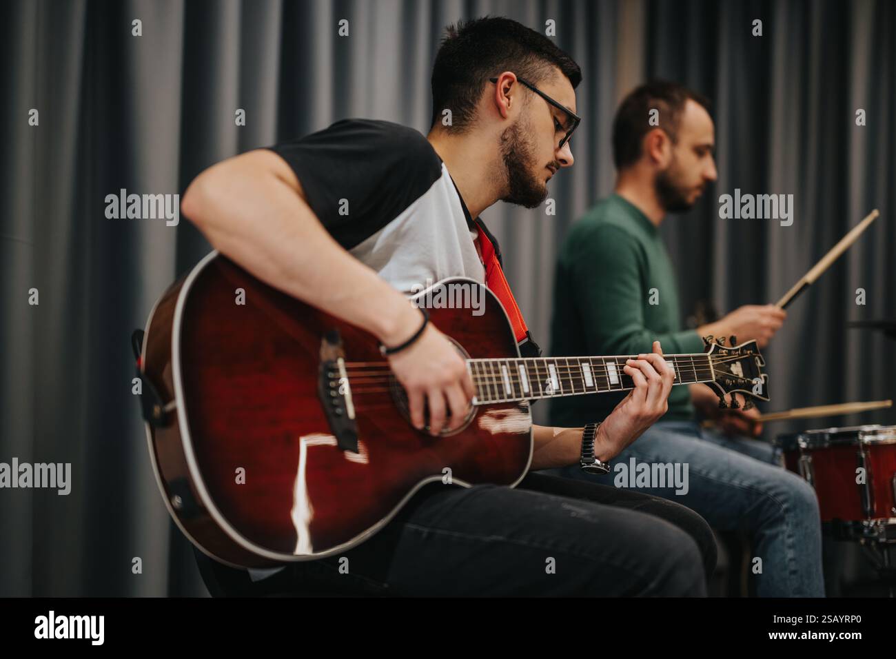 Two musicians performing in a studio with guitar and drums Stock Photo ...