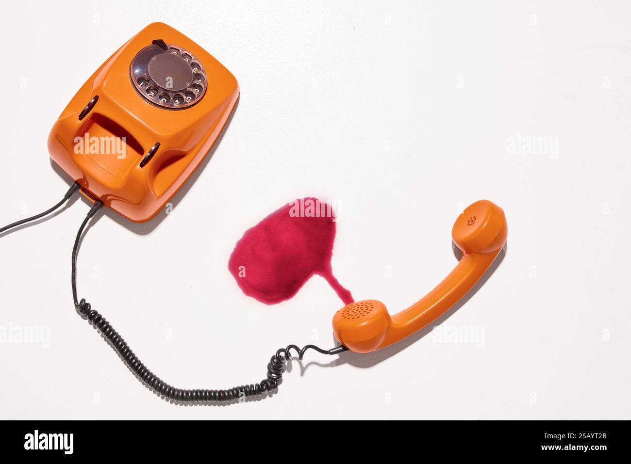 Orange rotary phone with disconnected receiver lies next to spilled red ...