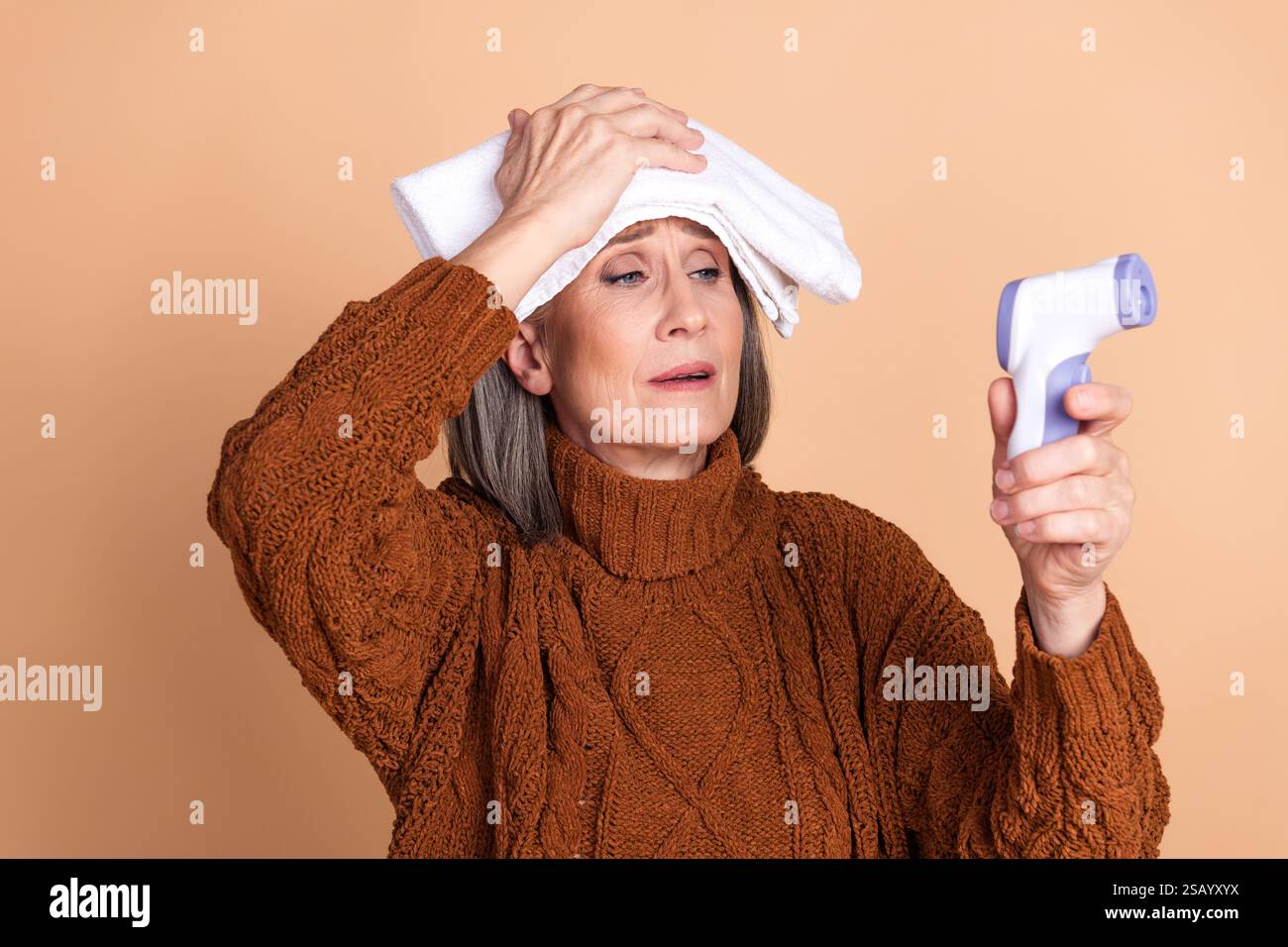 Elderly woman assessing fever with an infrared thermometer over a beige ...