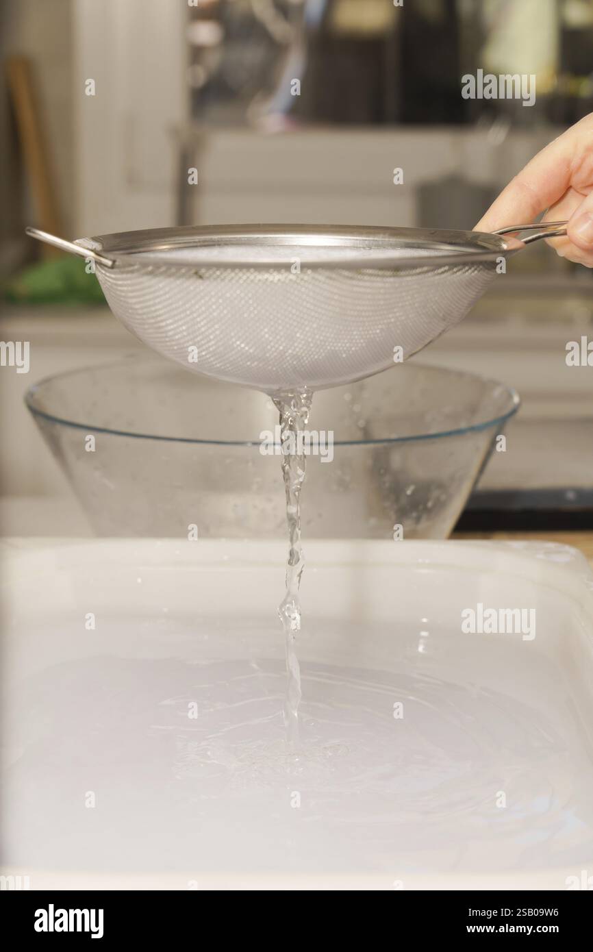 A woman's hand holding a strainer pouring water over a white pan Stock ...