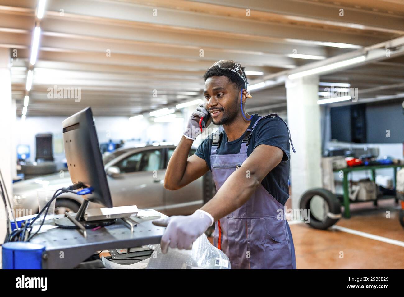 Young mechanic wearing gray uniform and protective glasses using ...