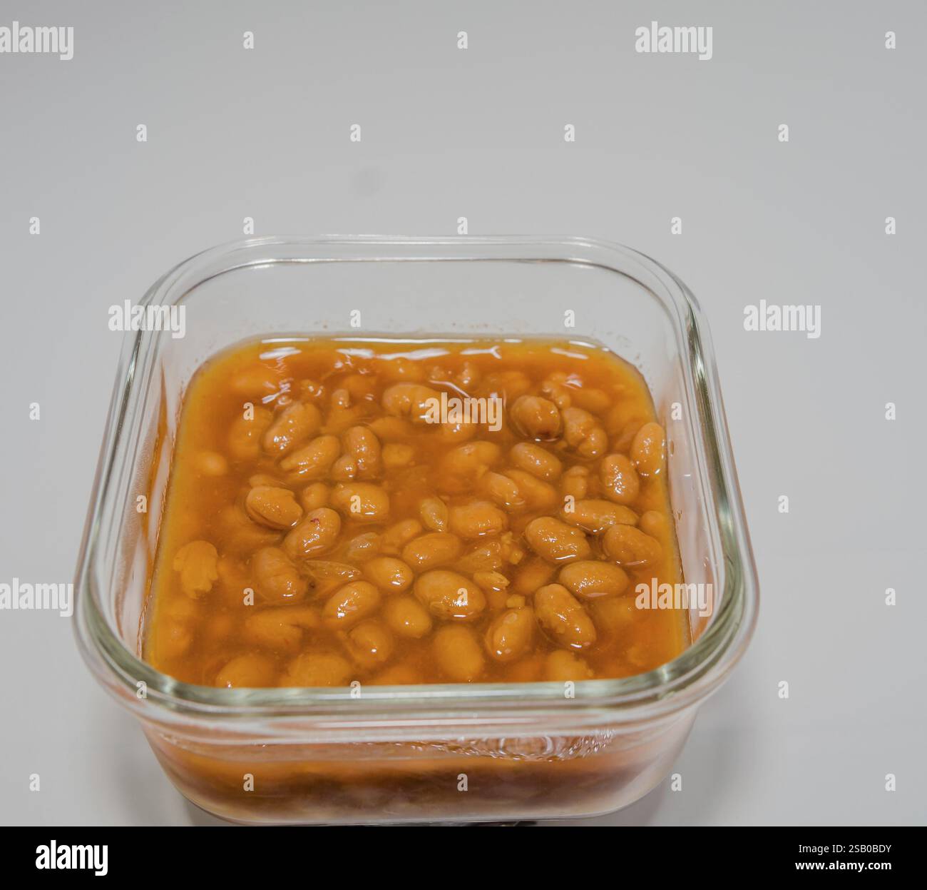 Glass container filled with baked beans in a rich sauce against a white ...