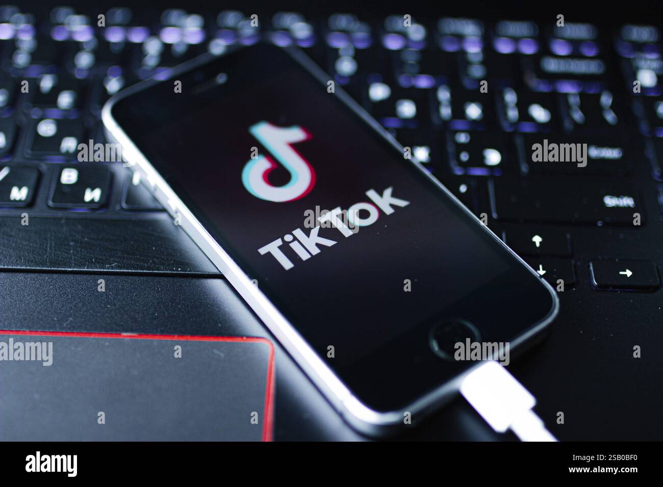 Phone on a laptop, showing the TikTok app logo while connected with a cable Stock Photo - Alamy