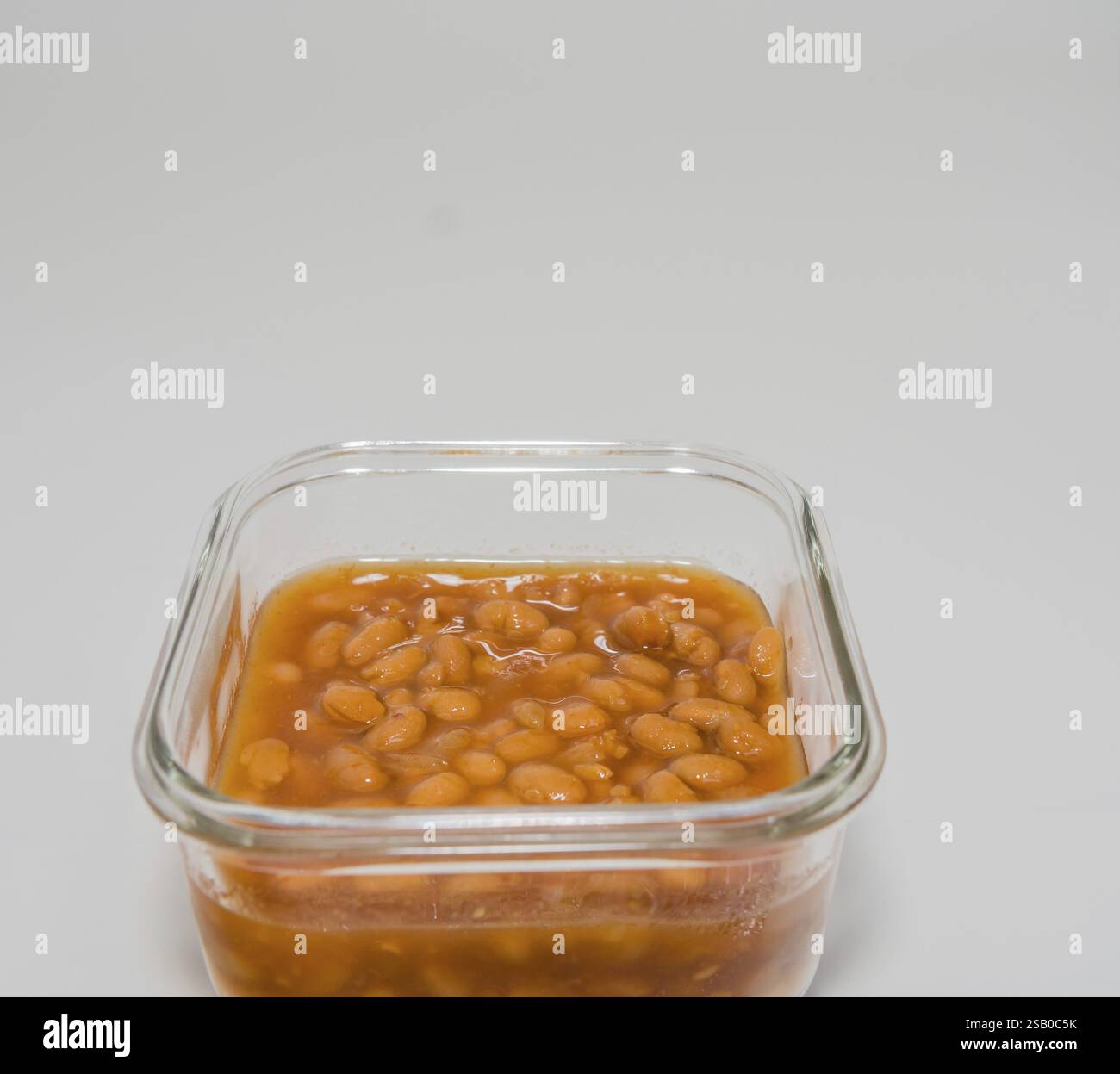 Glass container filled with baked beans in a rich sauce against a white ...