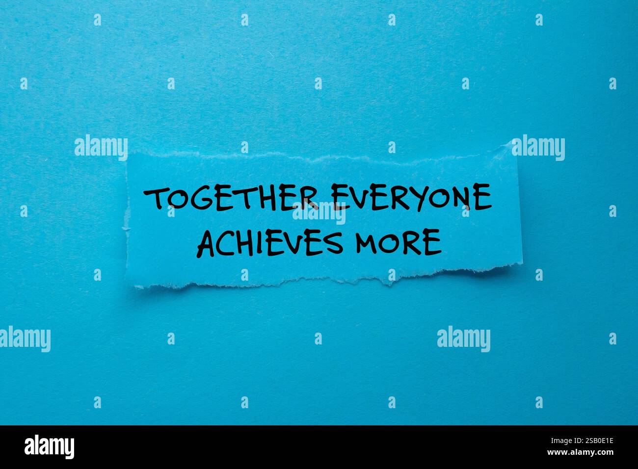 Together everyone achieves more message written on ripped torn paper piece on blue background ...