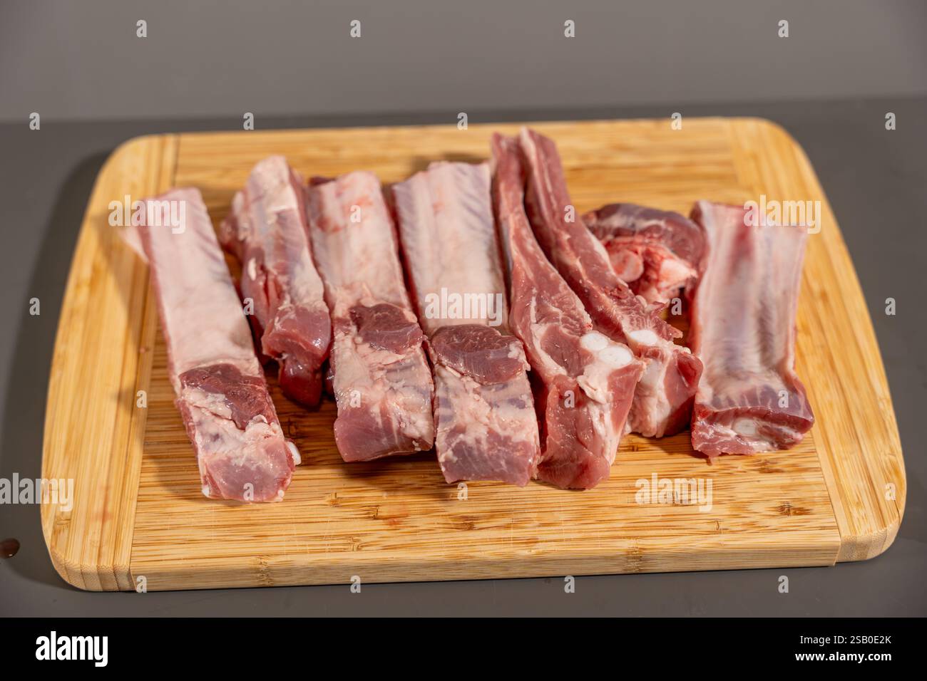 A slab of meat is cut into pieces and placed on a wooden cutting board ...