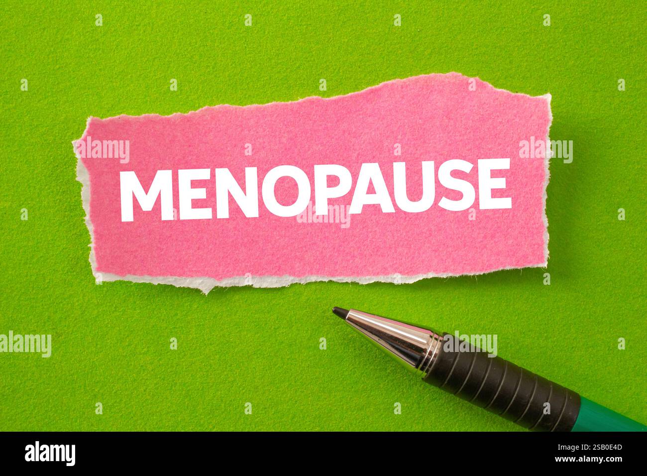 Menopause message written on ripped torn pink paper piece on green ...
