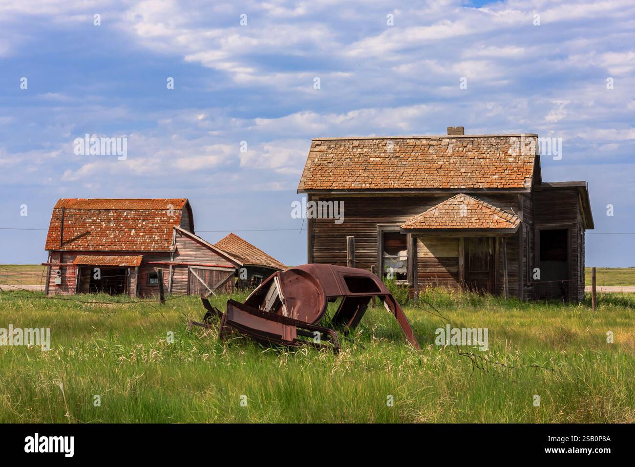 A rusting old car is sitting in a field next to a house. The scene is ...