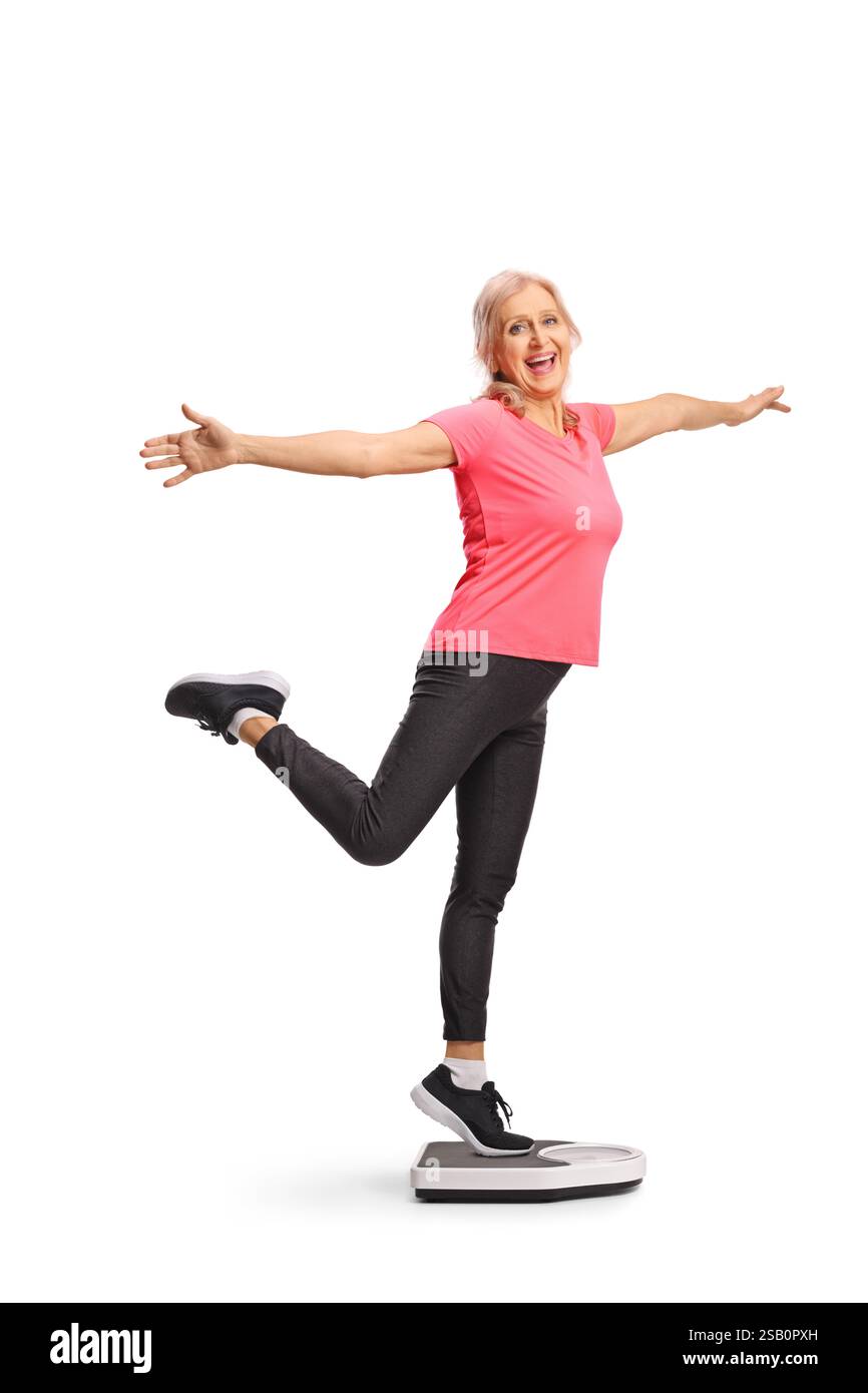 Smiling mature woman in sportswear dancing on a weight scale isolated ...