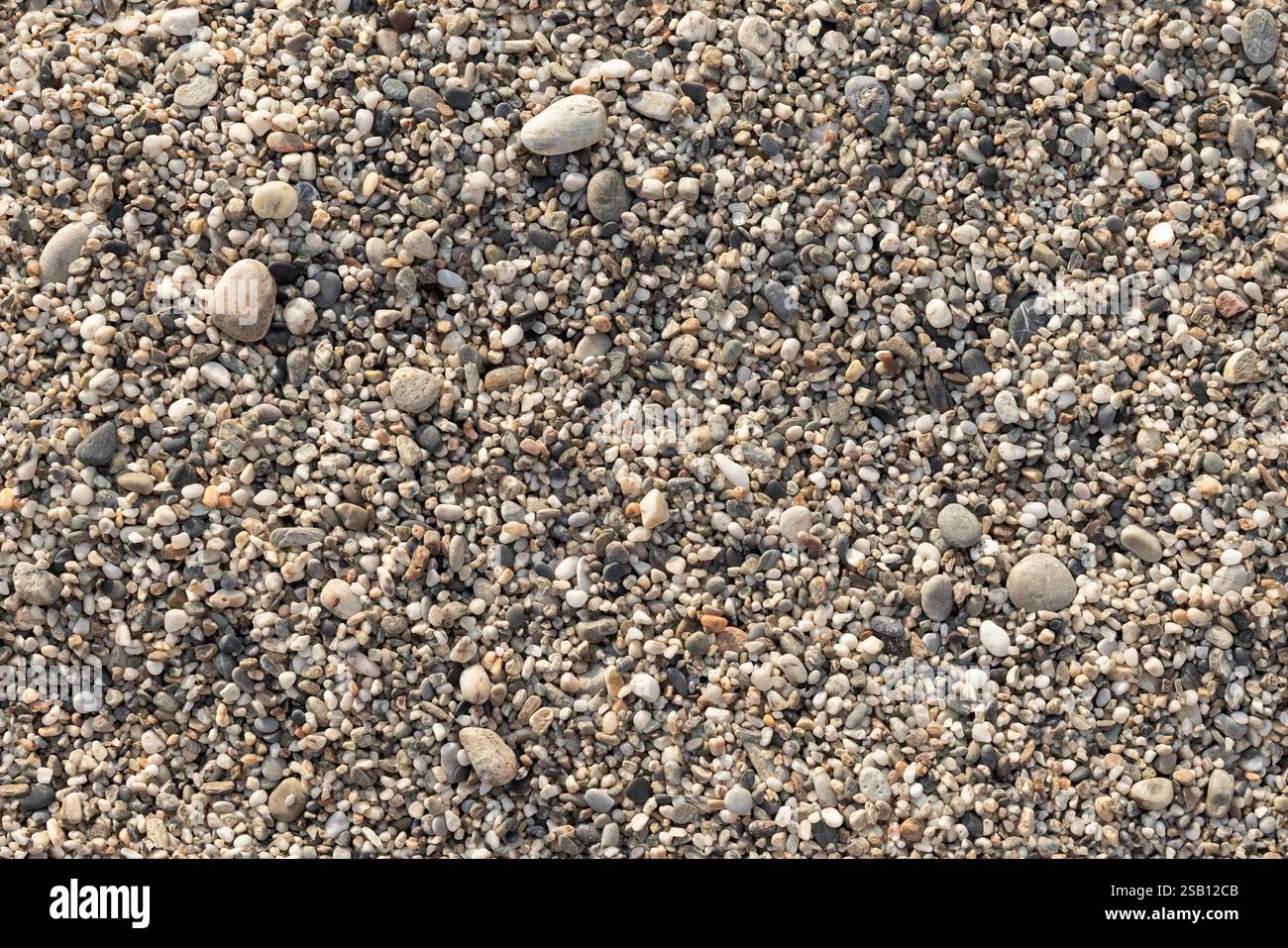 Coastal pebble mixed with coarse sand in a sunlight, top view, close-up ...