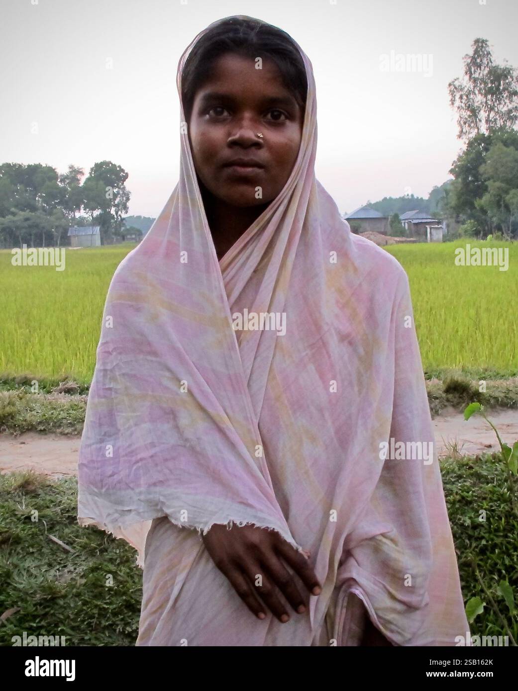 A young woman in a light cotton sari stands in a rural village near ...