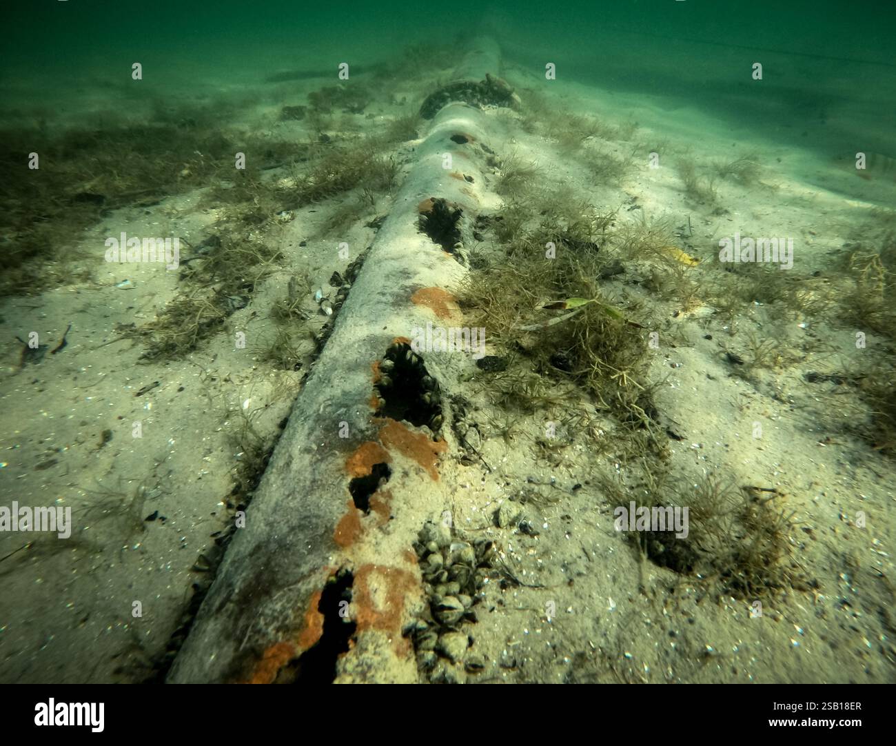 Underwater view of a rusty, damaged underwater pipe on a lakebed. The ...