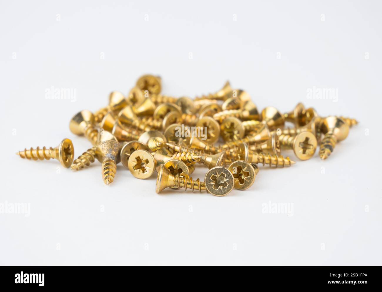 A pile of golden screws lies on a white surface ready for various ...