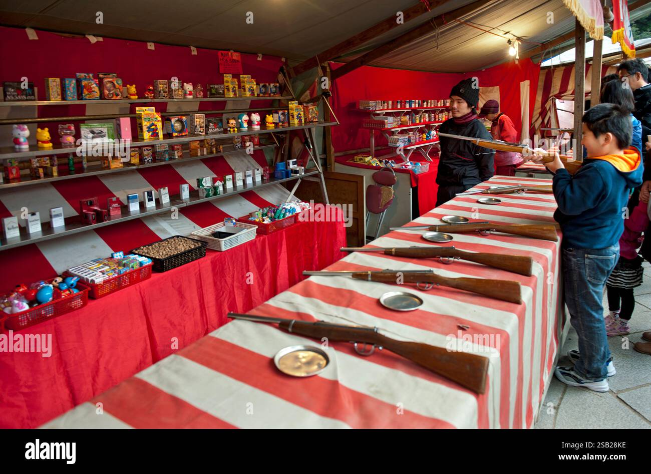 Boy taking aim with a rifle at a festival shooting gallery stand hoping ...