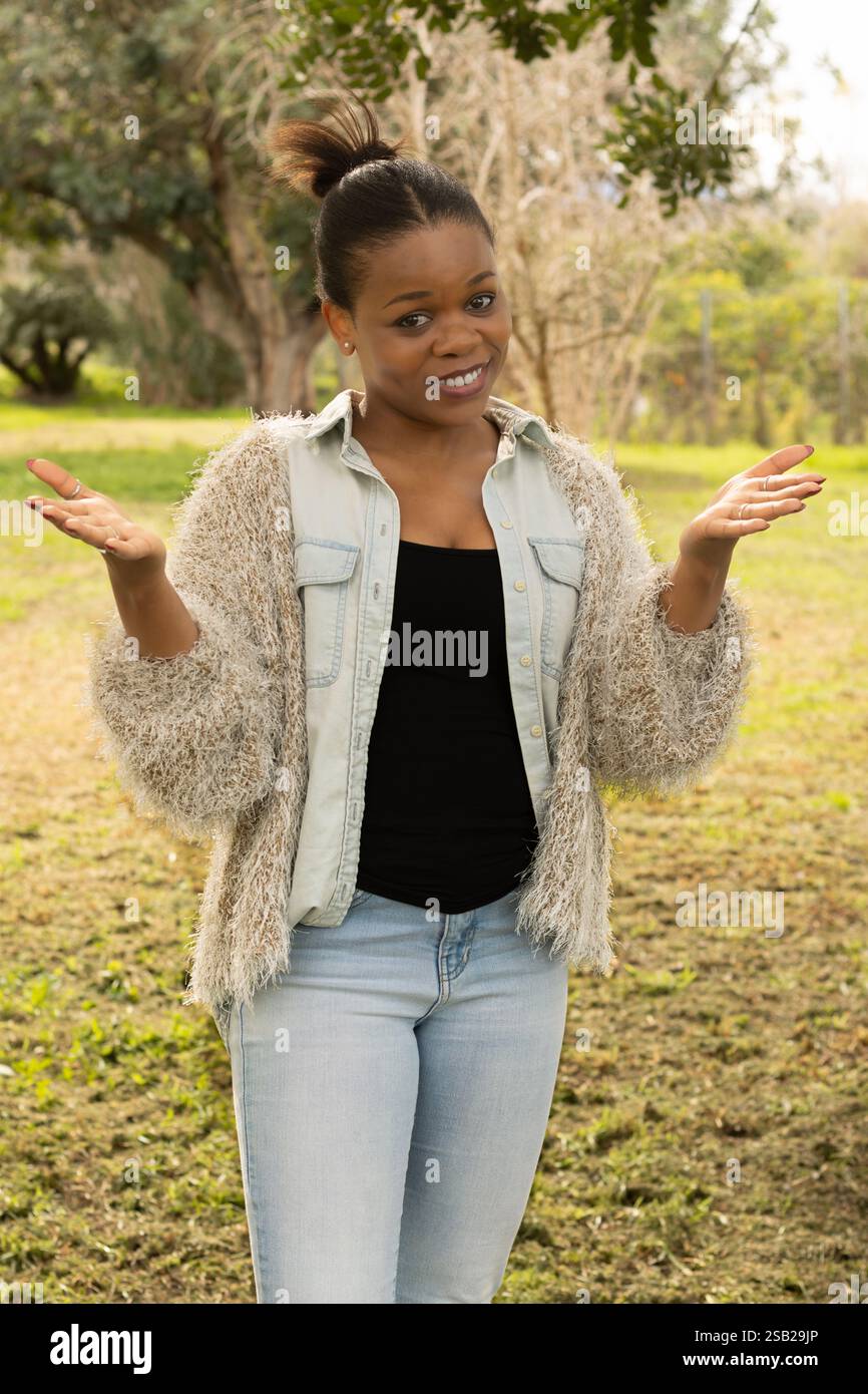 A black woman stands outside with her arms raised in a shrugging ...