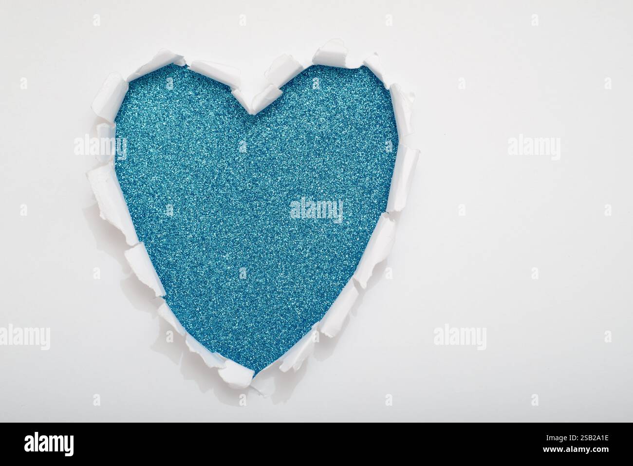 A heart-shaped hole is torn through white paper, revealing a teal ...